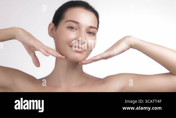 A stunning young woman with clear skin smiles while gently framing her ...