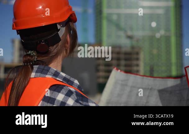 A diligent construction worker inspects blueprints while supervising a busy building site under ...