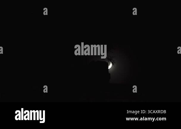 A new moon glows behind a house chimney, casting stark silhouettes and ...