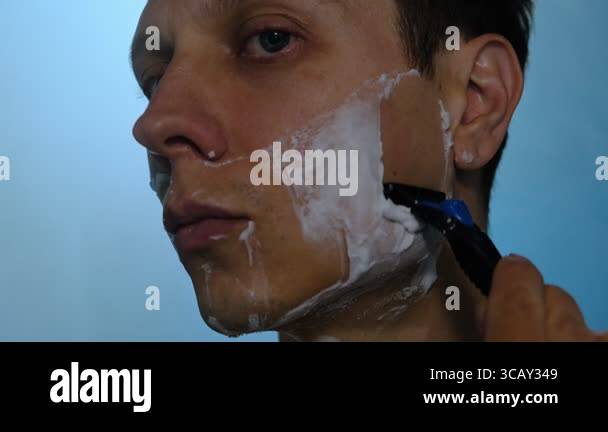 Young man begins shaving his face with a razor after applying shaving ...