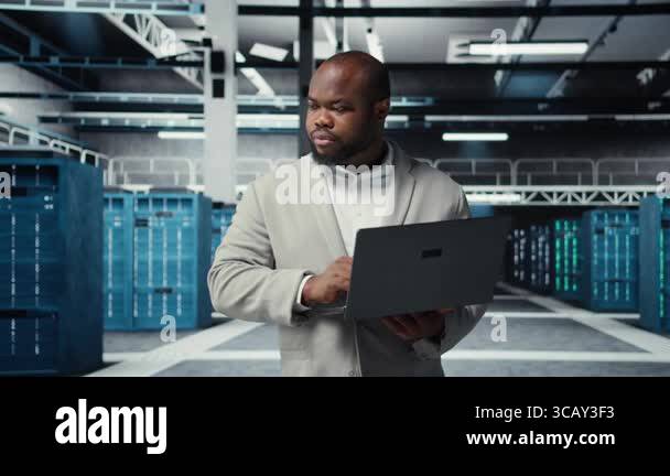 Technician walking in data center, using laptop to check hardware for system stability. Worker ...