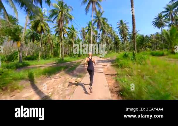 Cinematic FPV drone shot of fit woman running on path through tropical ...