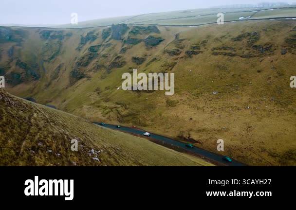 Cars driving along winding road through steep green valley. Vehicles ...