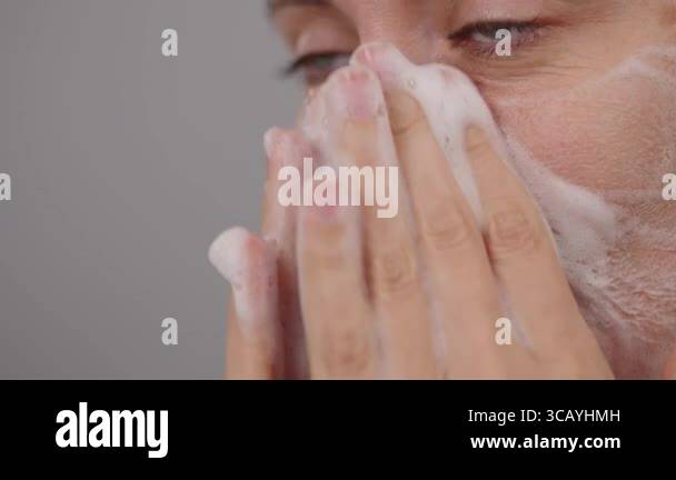 Extreme close-up of a female face. Woman applying cleansing foam gently ...