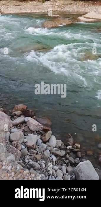 Clear water flows down a river surrounded by rocks and vegetation Stock ...