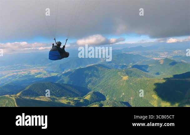 Paraglider flying high above green forested mountains beneath a ...