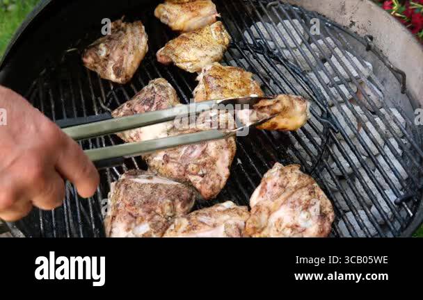 Using tongs to turn chicken thighs as they cook on a charcoal grill in ...