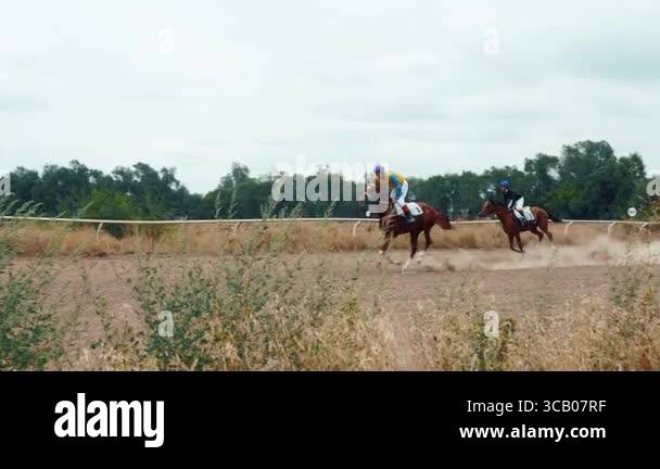 Two jockeys ride their racehorses on a dirt track in a competitive race ...
