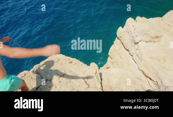 Man performing backflip jump off rocky cliff into deep blue sea in ...