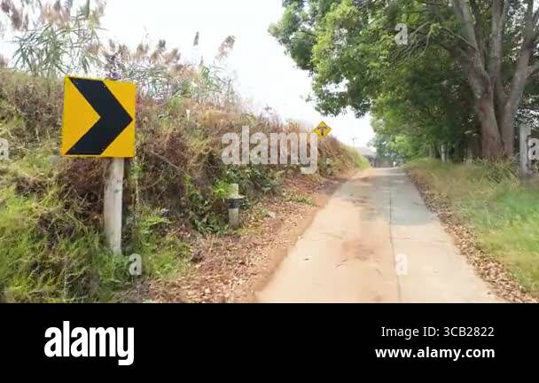 A yellow road sign with a directional arrow stands along a secondary ...