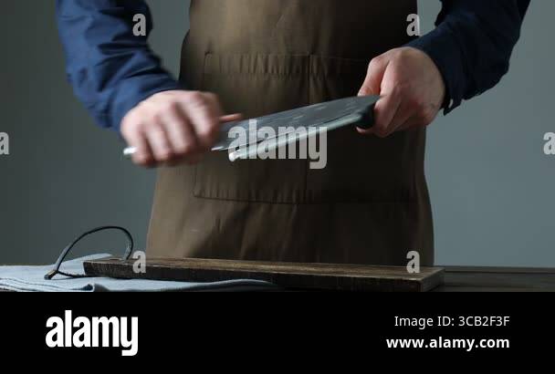 Man sharpening knife with sharpener at wooden table against grey ...