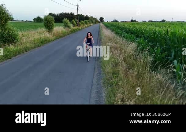 A person rides a bicycle along a quiet rural road surrounded by lush ...