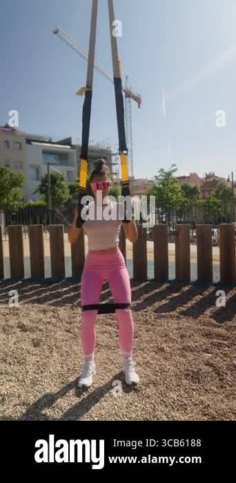 A fit woman is engaged in a suspension workout in a sunny outdoor park ...