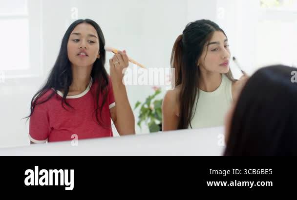 Female friends smiling into mirror, sharing brushes and applying gloss ...