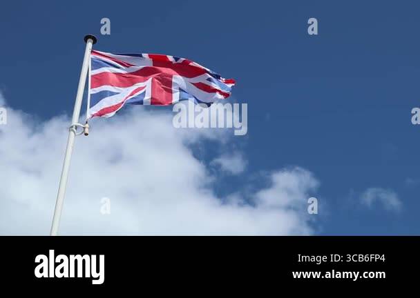 Union Jack flag flutters in the wind against a clear blue sky with soft ...