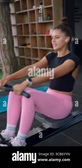 A fit woman vigorously exercises on a rowing machine in a modern gym ...