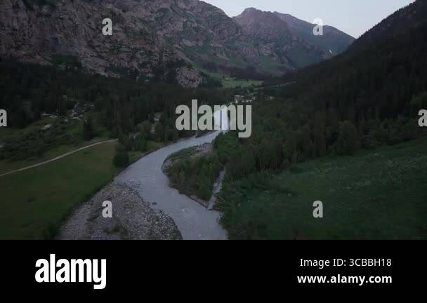 Dawn breaks over a tranquil mountain valley as a river meanders through ...
