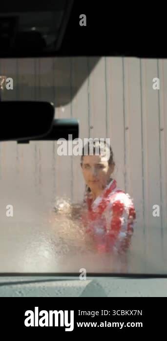 Car wash. A woman is washing a front windshield of the car with clean ...