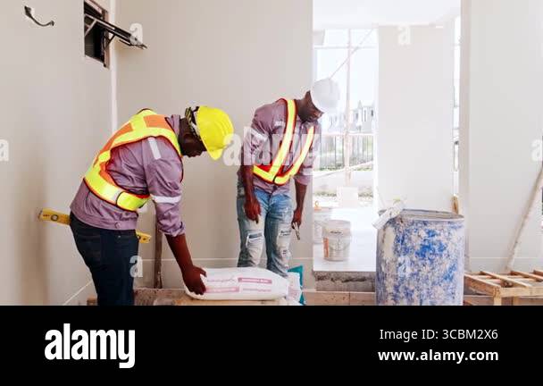 Two construction workers wearing safety vests and helmets work with ...