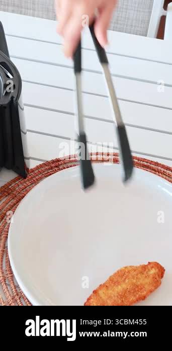 A person uses tongs to place crispy chicken pieces onto a white plate ...