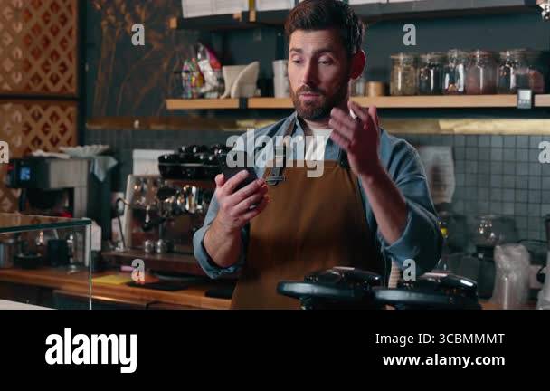Frustrated confused Caucasian barista man look screen mobile phone in ...