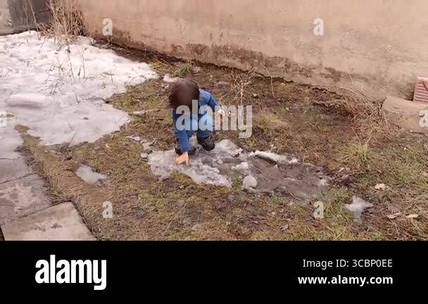 Young kid playing outdoors, stepping and jumping on muddy ground and ...