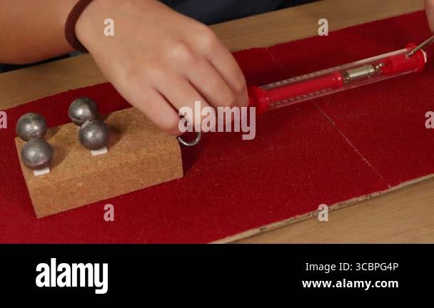 A hand uses a spring scale to measure force on a weighted block on ...