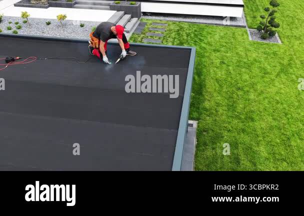 A skilled worker applies EPDM roofing material on a contemporary flat ...