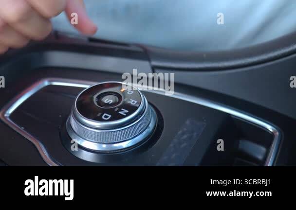 Close-up of hand turning gear shift knob in modern car interior. Driver ...