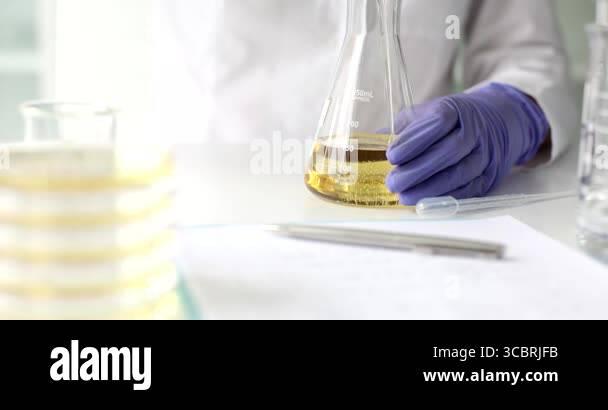 Scientist pours yellow liquid into transparent flask standing on white ...