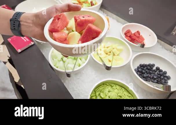 Closeup of man holding bowl adding fresh fruit from breakfast fruit ...