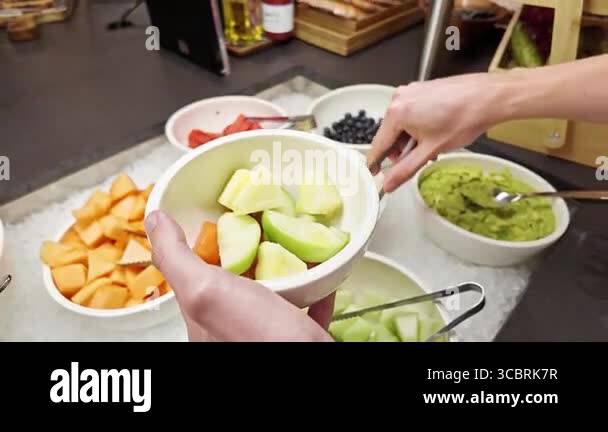 Man picks fresh fruits into bowl at hotel breakfast buffet with big ...