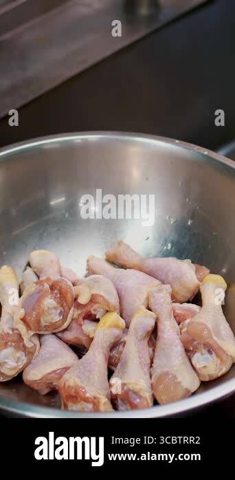 Close-up. cuisine worker, in protective gloves, washes raw chicken legs ...