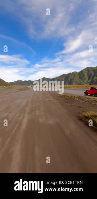 Cinematic FPV drone shot of red off-road vehicles driving across volcanic black sand plains near ...