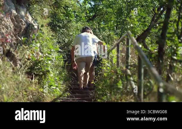 Older couple climbing outdoor forest path, walking up rustic stone ...