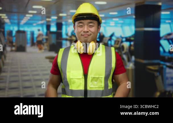 Man in gym wearing hard hat and reflective vest with headphones smiling ...
