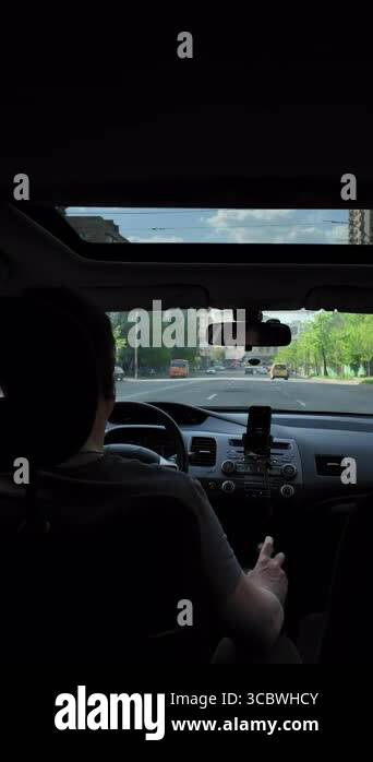 Footage from inside a vehicle showing a man driving on a city road. The ...