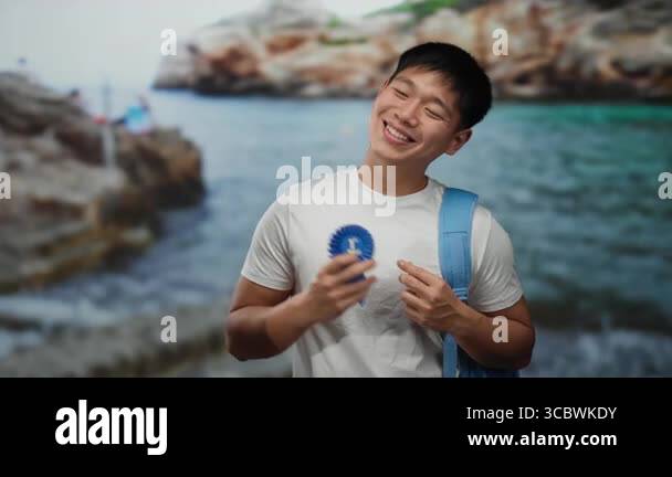 Young man with blue ribbon smiles joyfully on a scenic seaside, holding ...