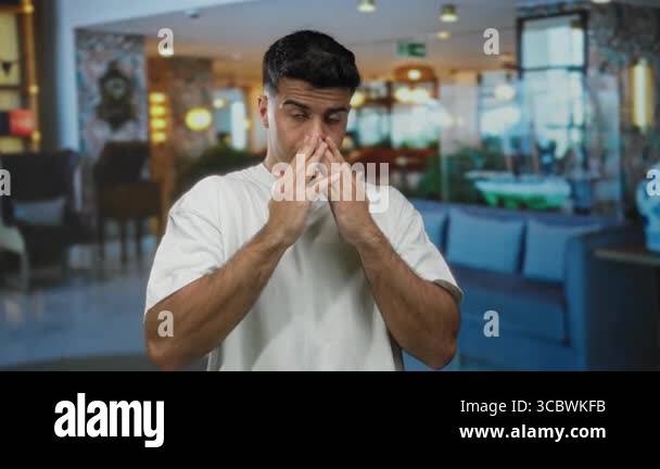 Handsome young man in casual white shirt gesturing indoors at a stylish ...