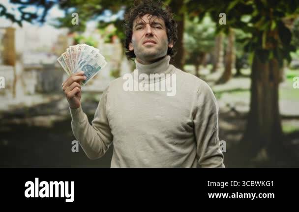 Hispanic man holding polish zloty banknotes in a park setting ...