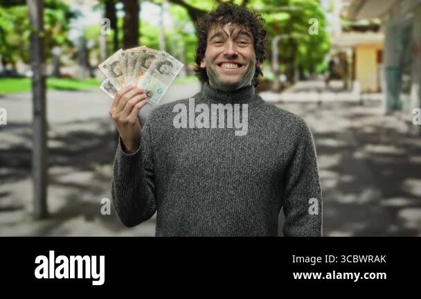 Hispanic man holding british pounds smiles outdoors on a city street ...