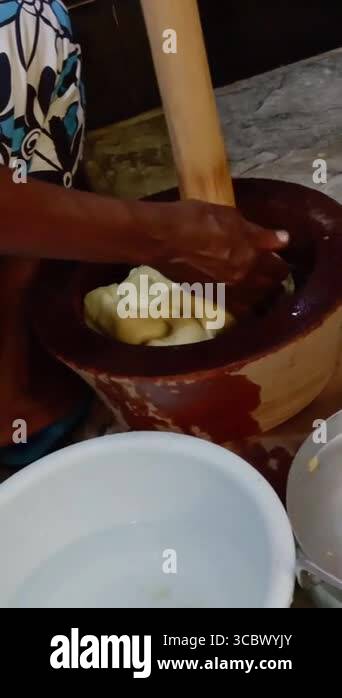 African woman turning yellow fufu, Ghanaian food, in brown wooden ...