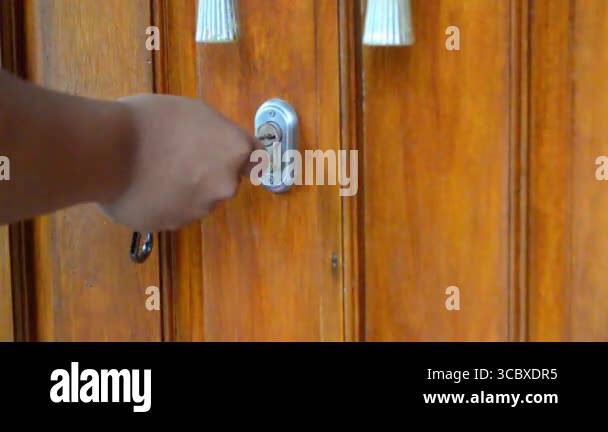 Close up of hand unlocking entrance door knobs with a key. Person using ...