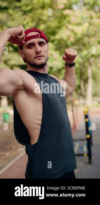 A muscular man wearing a black tank top and red baseball cap flexes his ...