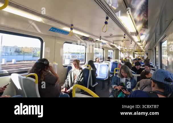Passengers on a Melbourne train during daylight, engaging with devices ...