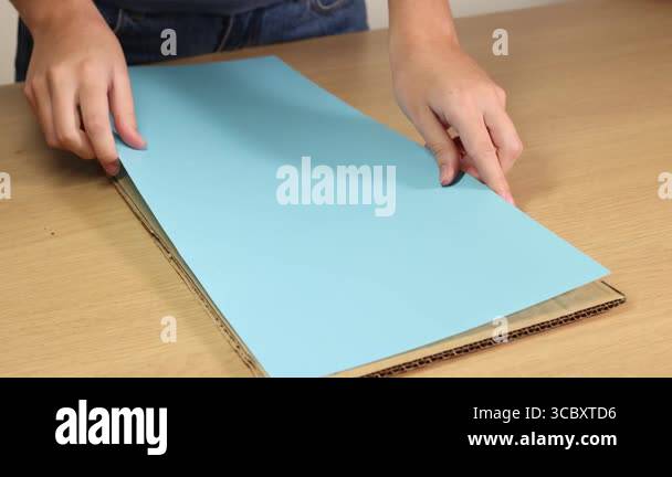 Hands methodically fold blue paper on a wooden table under soft ...