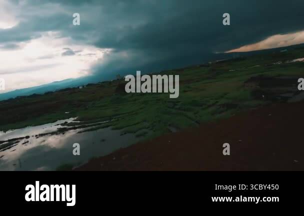 A dramatic landscape featuring dark storm clouds looming over a green ...