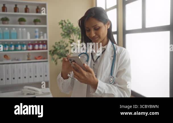 Woman wearing doctor attire smiling at phone inside clinical room ...