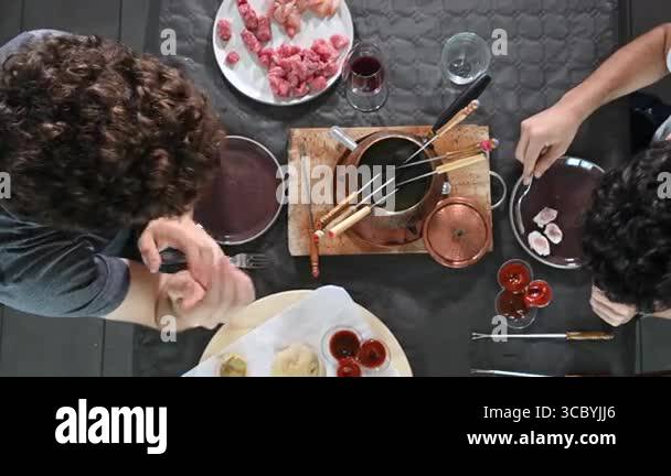 Footage of two friends at a table chatting while preparing and enjoying ...