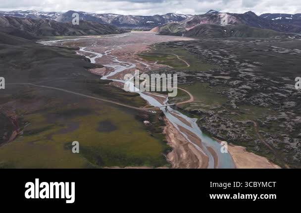 Aerial pan of an Icelandic valley with a winding river, a small bridge ...